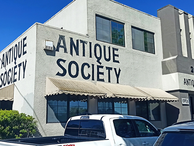 The iconic white facade of Antique Society stands proudly against the California blue sky, with outdoor vendors creating a festive marketplace atmosphere.