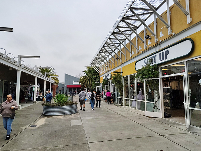 Shoppers stroll between colorful storefronts under an industrial-chic canopy, where the words "SUIT UP" aren't just a store name but a battle cry for discount warriors.