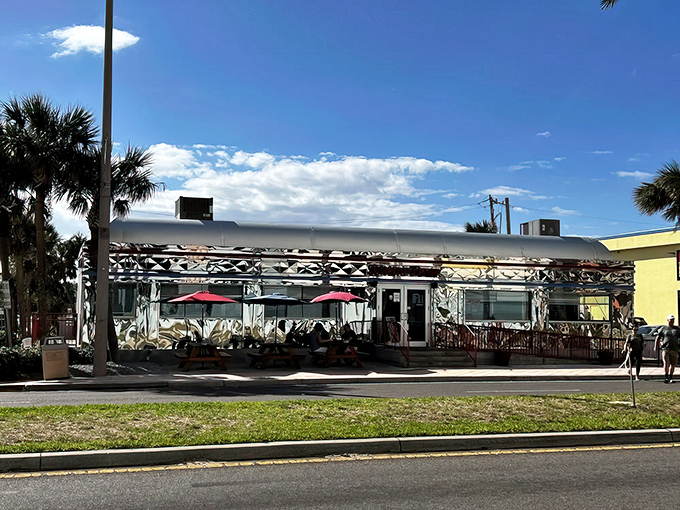 The gleaming silver exterior of Starlite Diner catches Florida sunshine like a time machine from the 1950s, complete with palm trees and red umbrellas for that perfect retro vibe.