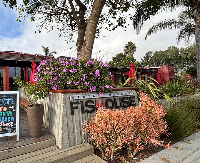 The entrance to seafood paradise – where vibrant bougainvillea and coastal plants frame a weathered wood exterior that practically whispers, "Come in, the fish is waiting."
