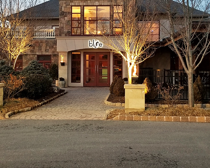 Blue Grillhouse greets guests with its warm stone exterior, glowing lights, and signature blue sign—hinting at the culinary delights waiting inside.