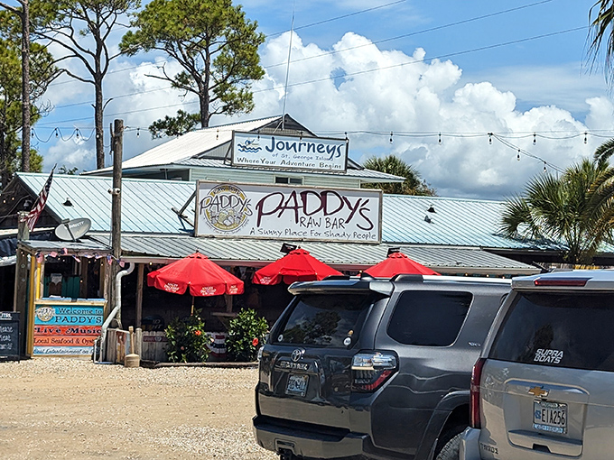 The weathered metal roof and "Sunny Place for Shady People" sign tell you everything you need to know&mdash;authenticity awaits beneath those red umbrellas.