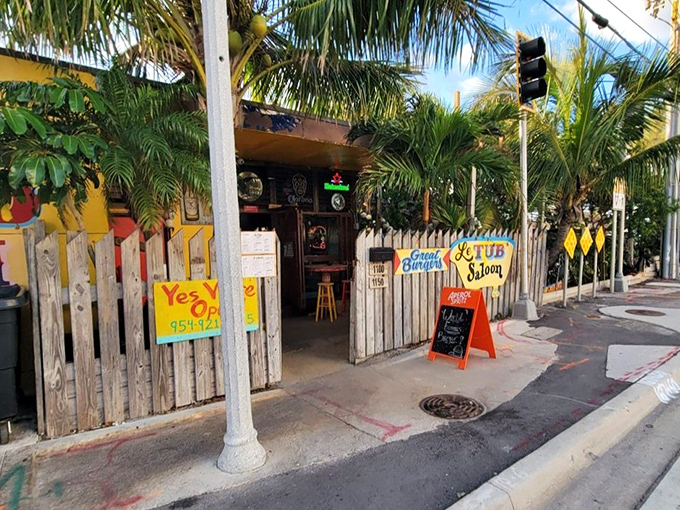 The unassuming entrance to Le Tub Saloon, where weathered wooden fences and colorful signs promise "Great Burgers" and a truly Floridian escape from pretension.