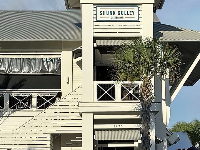 Coastal elegance meets laid-back charm at Shunk Gulley's pristine white exterior, where those blue umbrellas practically whisper "come sit a while."