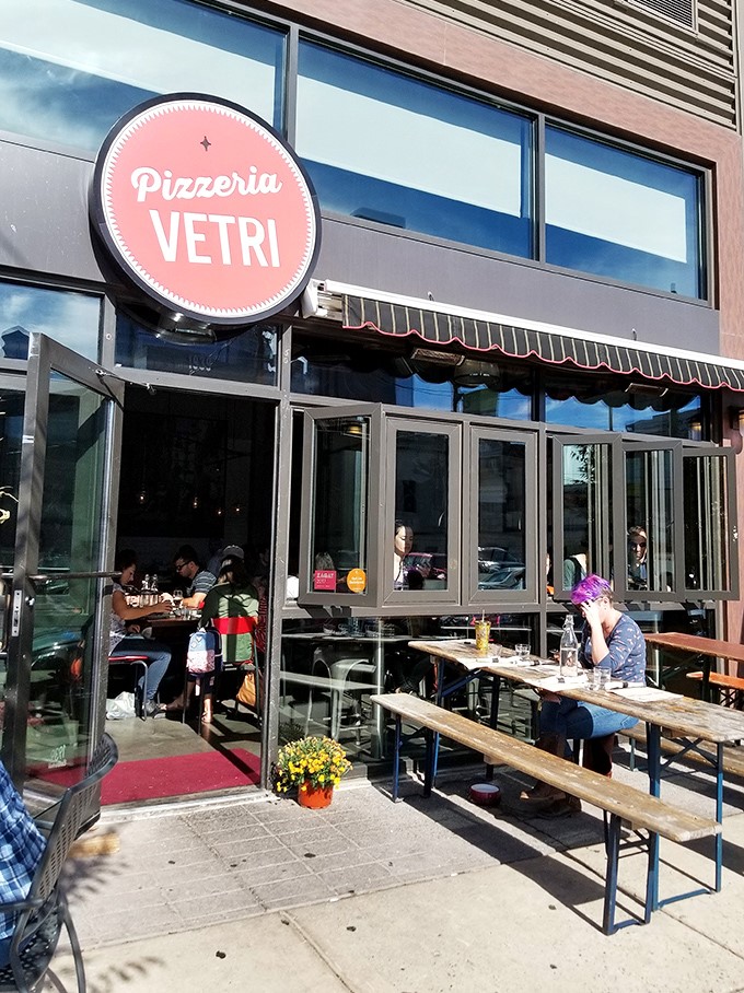 The iconic pink sign beckons pizza lovers to Pizzeria Vetri, where outdoor tables invite you to enjoy a slice of heaven under Philadelphia skies.