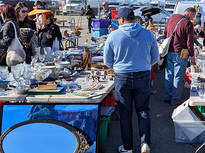 Treasure hunters scan tables piled with vintage glassware and collectibles. The thrill of the hunt is palpable in the morning light.
