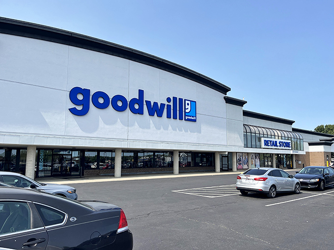 The iconic blue Goodwill sign beckons like a lighthouse for bargain hunters, promising treasures within its spacious confines.