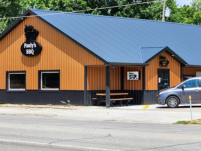 Pauly's BBQ stands proudly with its blue metal roof and wooden siding, like a beacon of smoky goodness in Arthur's Amish country.