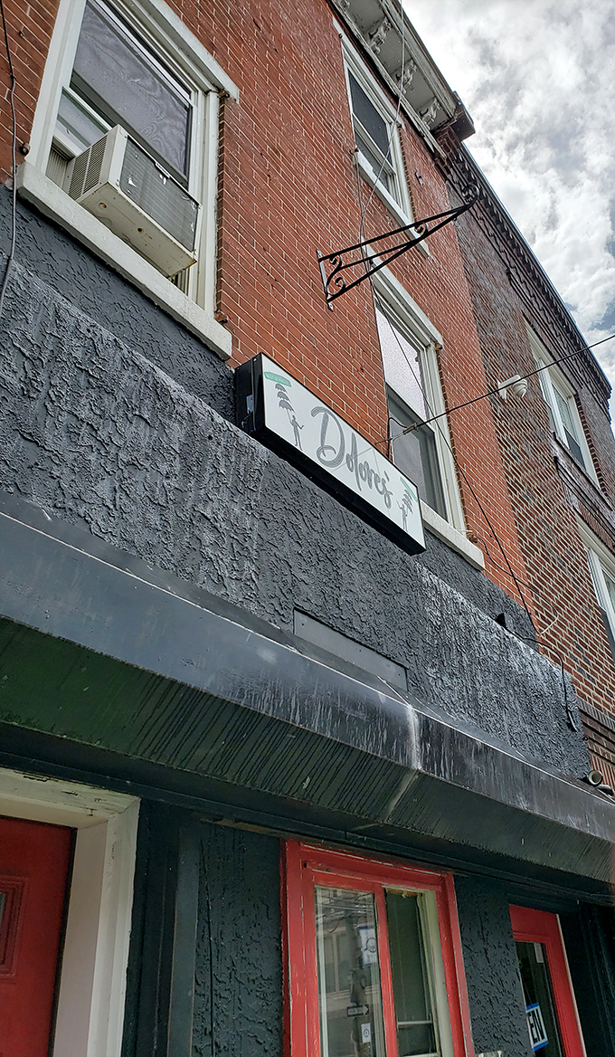 The unassuming exterior of Dolores' Deli, where that vibrant red door serves as Philadelphia's version of the yellow brick road to sandwich paradise.