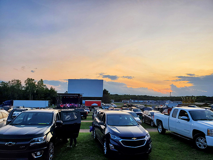 Cars gather under a pastel sunset sky, waiting for darkness to transform this field into a communal theater of dreams and buttery popcorn.