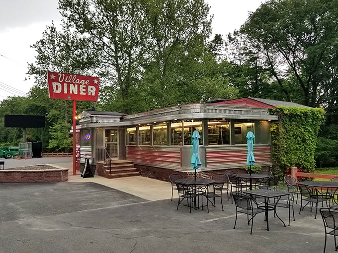 The classic stainless steel exterior of Village Diner gleams like a time capsule from the golden age of roadside dining, complete with that iconic red sign beckoning hungry travelers.