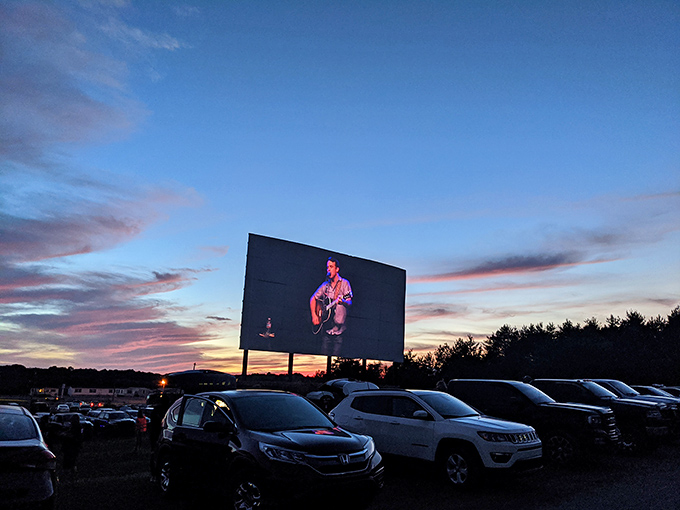 Cars gather under a pastel sunset sky, waiting for darkness to transform this field into a communal theater of dreams and buttery popcorn.