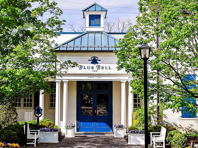 The historic Blue Bell Inn stands proudly in Pennsylvania sunshine, its whitewashed exterior and classic black shutters whispering stories from centuries past.
