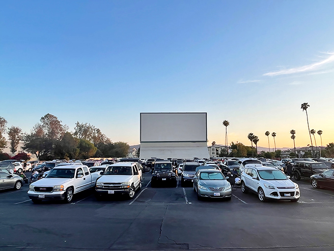 Cars lined up like eager moviegoers from decades past, the massive white screen standing ready for cinematic magic as palm trees frame the California sunset.
