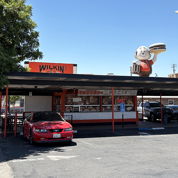 The iconic orange and white exterior of Wilkin's Drive-In stands like a time capsule under the Central Valley sun, complete with its cheerful burger-toting mascot.