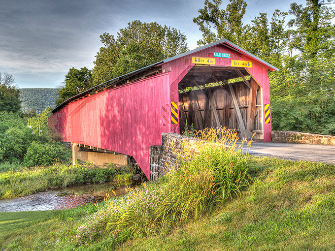 Nature's perfect frame for Adair's crimson beauty, where Sherman's Creek whispers stories beneath wooden beams that have witnessed generations of travelers.