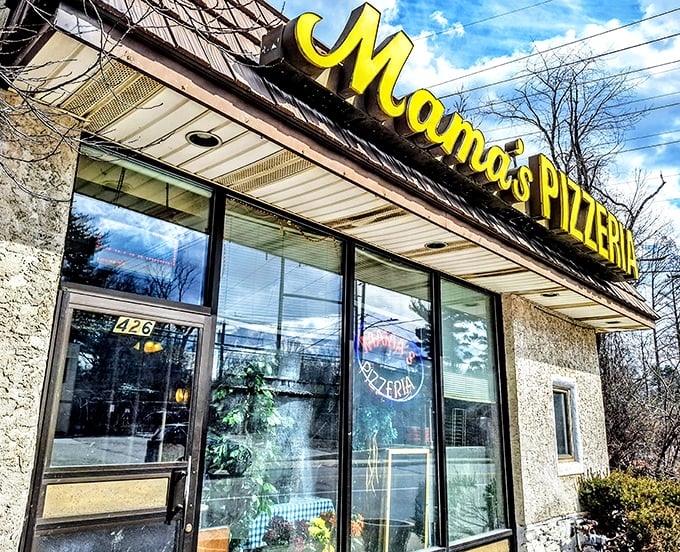 The iconic yellow Mama's Pizzeria sign stands out against the blue sky, with cherry blossoms adding a touch of natural beauty to this culinary landmark.