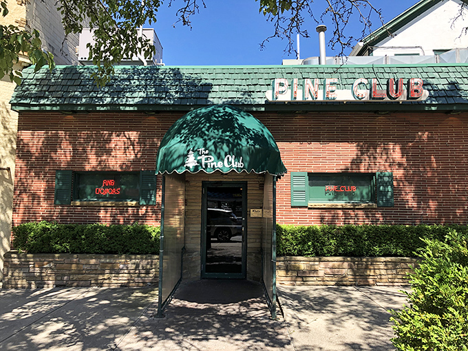 The iconic green-trimmed brick exterior of The Pine Club stands as a beacon for steak lovers, its vintage sign promising timeless delights within.