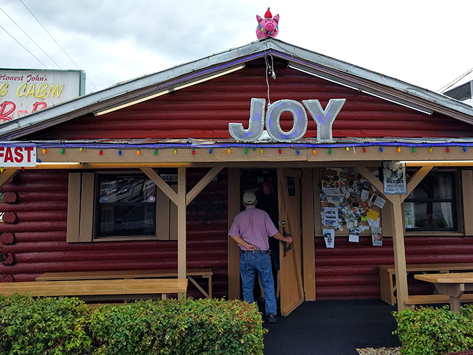 The pink pig perched atop this rustic log cabin isn't just decoration—it's a beacon of barbecue bliss calling hungry travelers to experience the "JOY" of authentic Florida BBQ.