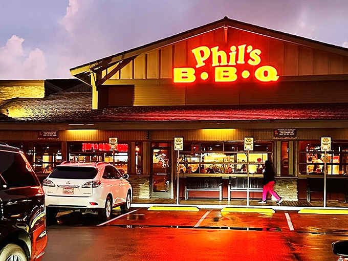 The neon glow of Phil's BBQ sign beckons hungry travelers like a barbecue lighthouse, promising smoky salvation after a long day.