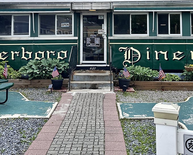 The emerald green exterior of Peterborough Diner beckons like a time machine disguised as a railroad car, complete with patriotic planters guarding the entrance.