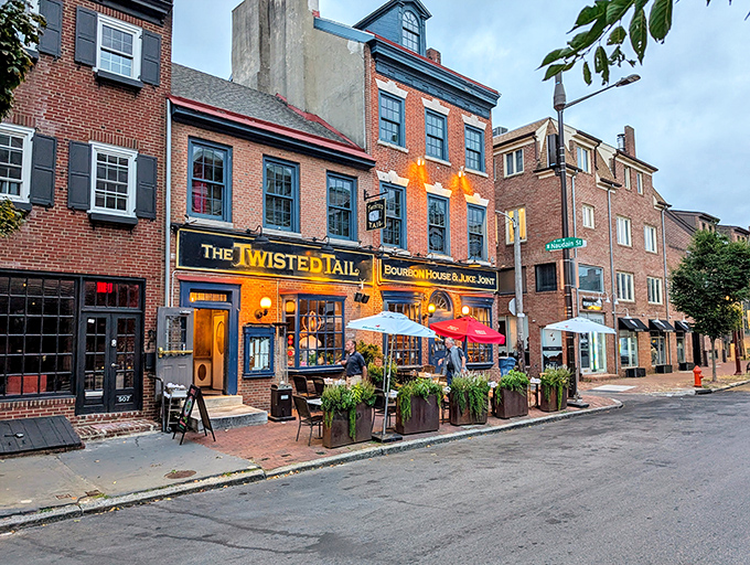 The historic brick fa&ccedil;ade of The Twisted Tail glows with welcome at dusk, its red umbrellas beckoning like culinary lighthouses in Philadelphia's Society Hill.