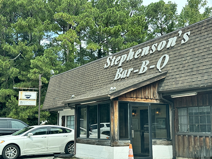 The unassuming exterior of Stephenson's Bar-B-Q stands like a barbecue beacon among towering pines, promising smoky treasures within.