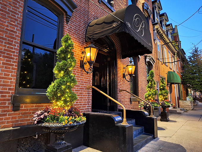 Victorian elegance meets culinary excellence at The Belvedere Inn's entrance, where twinkling lights and lush greenery welcome you to Lancaster's dining gem.