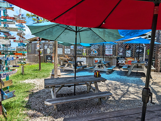The weathered metal roof and "Sunny Place for Shady People" sign tell you everything you need to know&mdash;authenticity awaits beneath those red umbrellas.