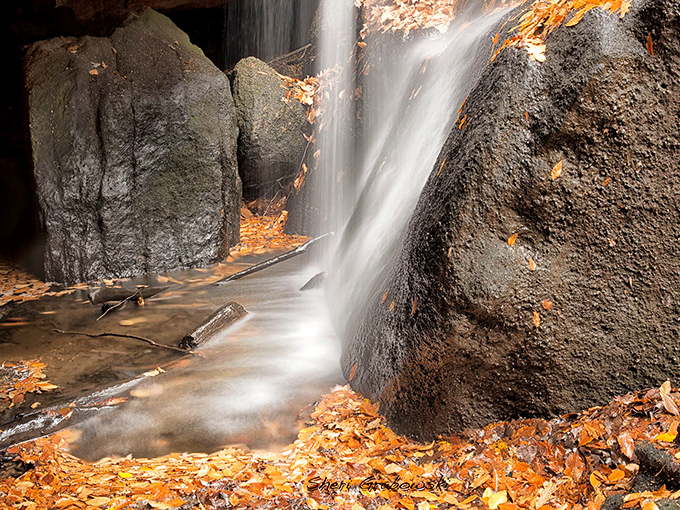 Nature's own watercolor masterpiece &ndash; autumn leaves frame this silky cascade as it tumbles between ancient rocks, creating a moment of perfect tranquility.
