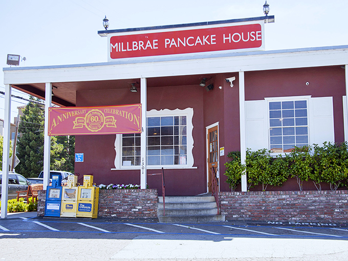 The iconic red exterior of Millbrae Pancake House stands like a beacon of breakfast hope, palm trees swaying as if to say "pancakes this way!"