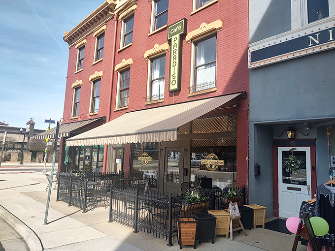 The vibrant red brick facade of Cafe Paradiso stands proudly on Monument Square, its awning and outdoor seating beckoning like an old friend with good news to share.