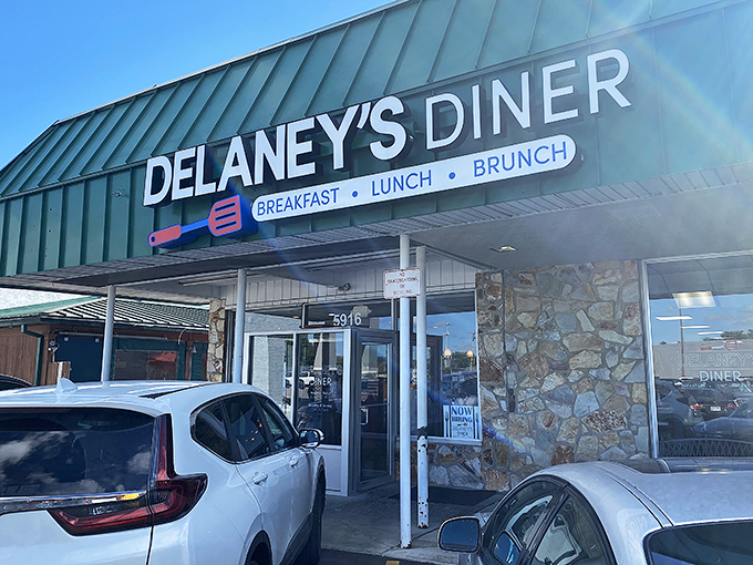 The distinctive green roof and stone facade of Delaney's Diner stands as a beacon for breakfast enthusiasts. That spatula sign promises delicious things await inside.