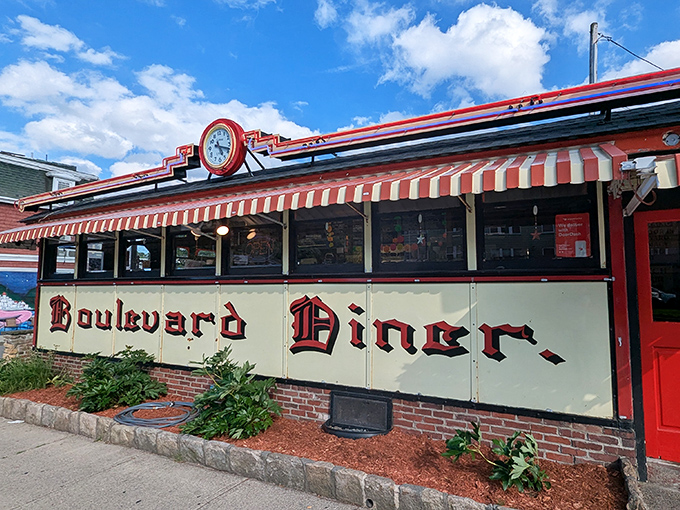 The classic red and cream exterior of Boulevard Diner stands like a time capsule of Americana, complete with vintage clock and striped awning inviting hungry travelers inside.