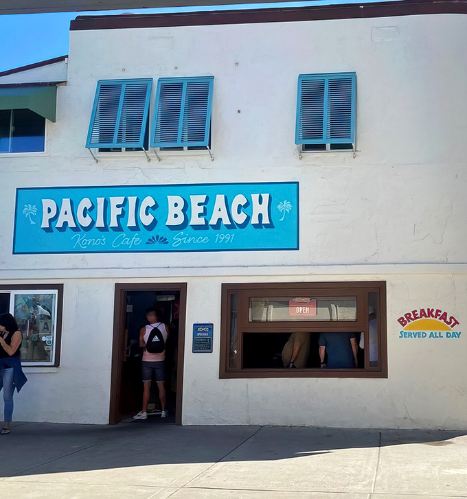 The iconic white-walled corner building with blue trim stands like a beacon for breakfast pilgrims. Palm trees sway overhead as if applauding your excellent dining choice.