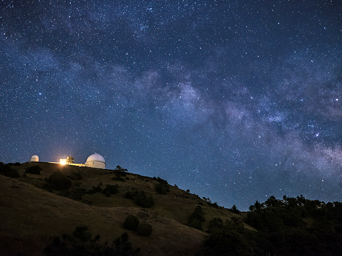 Starlight magic at its finest! The observatory's iconic white domes stand sentinel against a twilight sky, with a laser beam piercing the heavens like nature's own exclamation point.