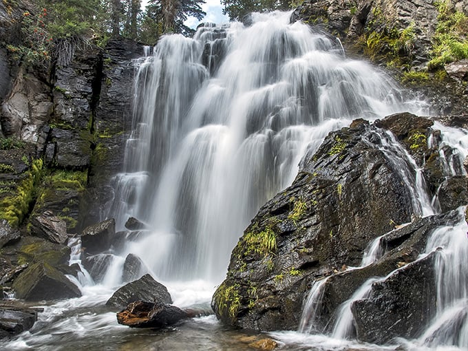 The waterfall's silky white curtain against dark volcanic rock creates nature's perfect high-contrast photograph, no filter required.