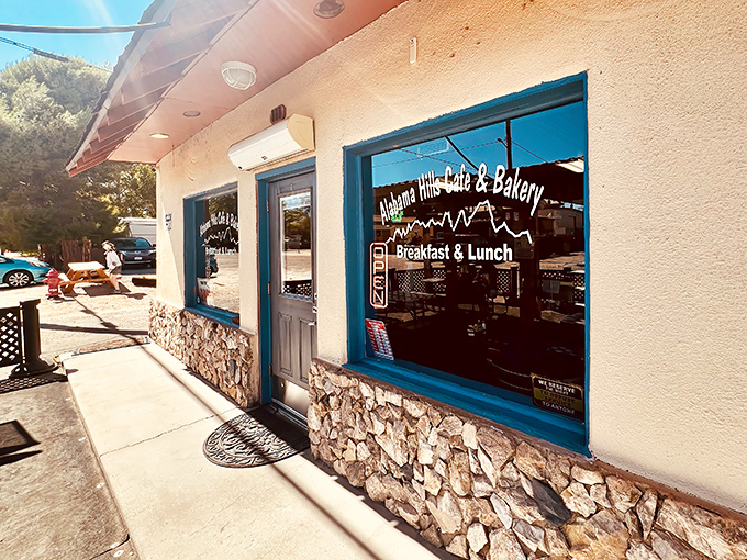 The unassuming exterior of Alabama Hills Cafe & Bakery, where culinary magic happens behind that blue-trimmed facade and stone foundation.