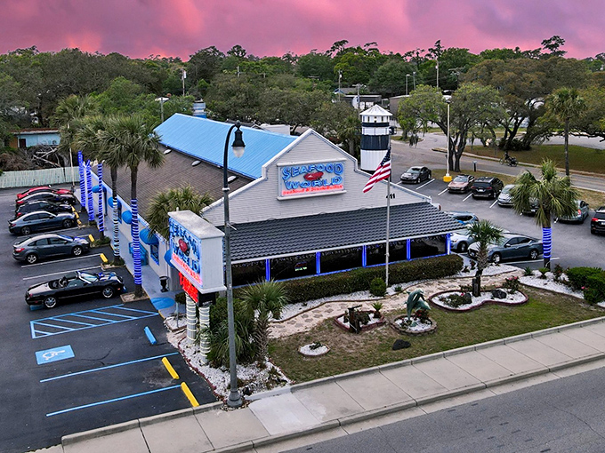 The iconic white-sided building with its bold blue signage stands like a beacon for seafood lovers, palm trees swaying in welcome.
