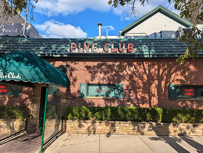 The iconic green-trimmed brick exterior of The Pine Club stands as a beacon for steak lovers, its vintage sign promising timeless delights within.