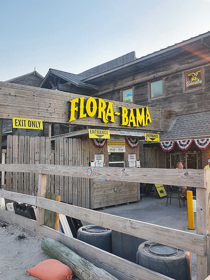 The weathered wooden exterior of Flora-Bama stands proudly on the state line, its bright yellow signage a beacon for hungry travelers seeking coastal treasures.