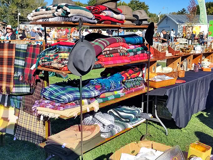 Colorful wool blankets stacked high like a textile rainbow. Each plaid pattern tells a different story, with a lone gray hat standing sentinel over this cozy kingdom.