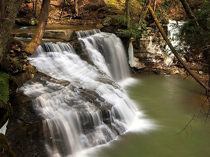 Sunlight filters through the forest canopy, highlighting the waterfall's graceful descent &ndash; a hidden Pennsylvania treasure worth every step of the journey.