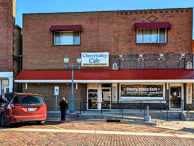 The brick facade and cherry-red awning of Cherry Valley Cafe stands as a beacon of breakfast hope on a quiet Illinois street.