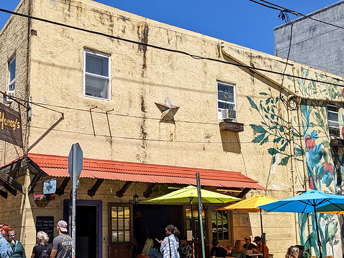 The weathered wooden sign against that mustard-yellow exterior says it all: unpretentious, welcoming, and promising something far better than its humble appearance suggests.