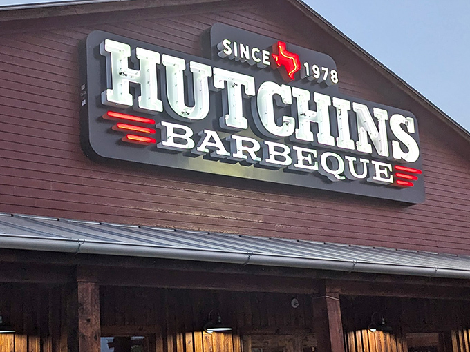 The iconic Hutchins BBQ sign glows like a beacon of smoky hope for hungry travelers. Texas barbecue paradise since 1978.