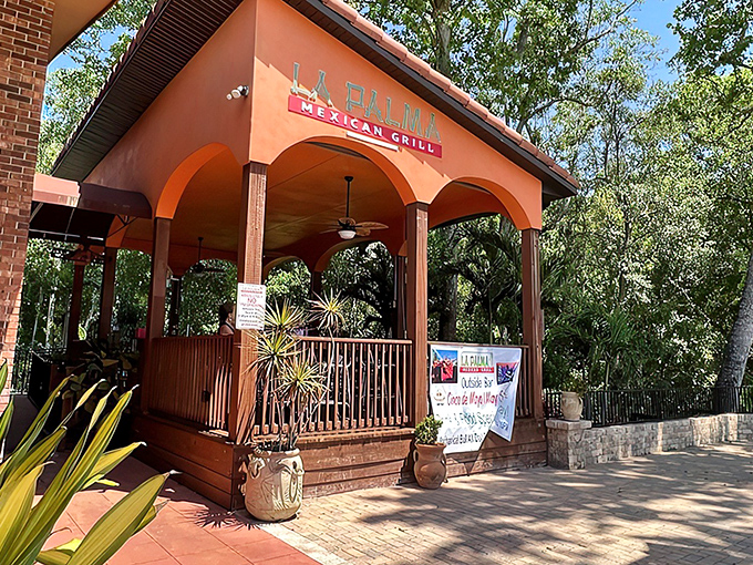 The terracotta-colored entrance beckons like a sunset invitation, promising authentic flavors behind those wooden railings and tropical plants.