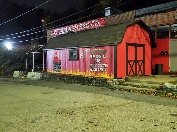 The little red barn of barbecue dreams stands out like a meat beacon in the night, promising smoky delights within those flame-painted walls.