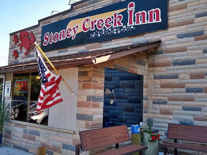 The stone facade of Stoney Creek Inn welcomes seafood pilgrims with its iconic red crab sign and American flag &ndash; Maryland hospitality in architectural form.