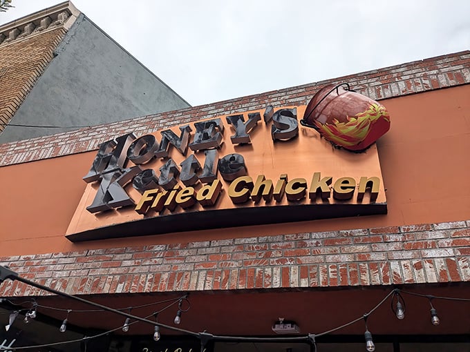 The bold sign of Honey's Kettle Fried Chicken, complete with a fiery kettle bucket and rustic brick trim, draws you in with promises of crispy, golden comfort food.